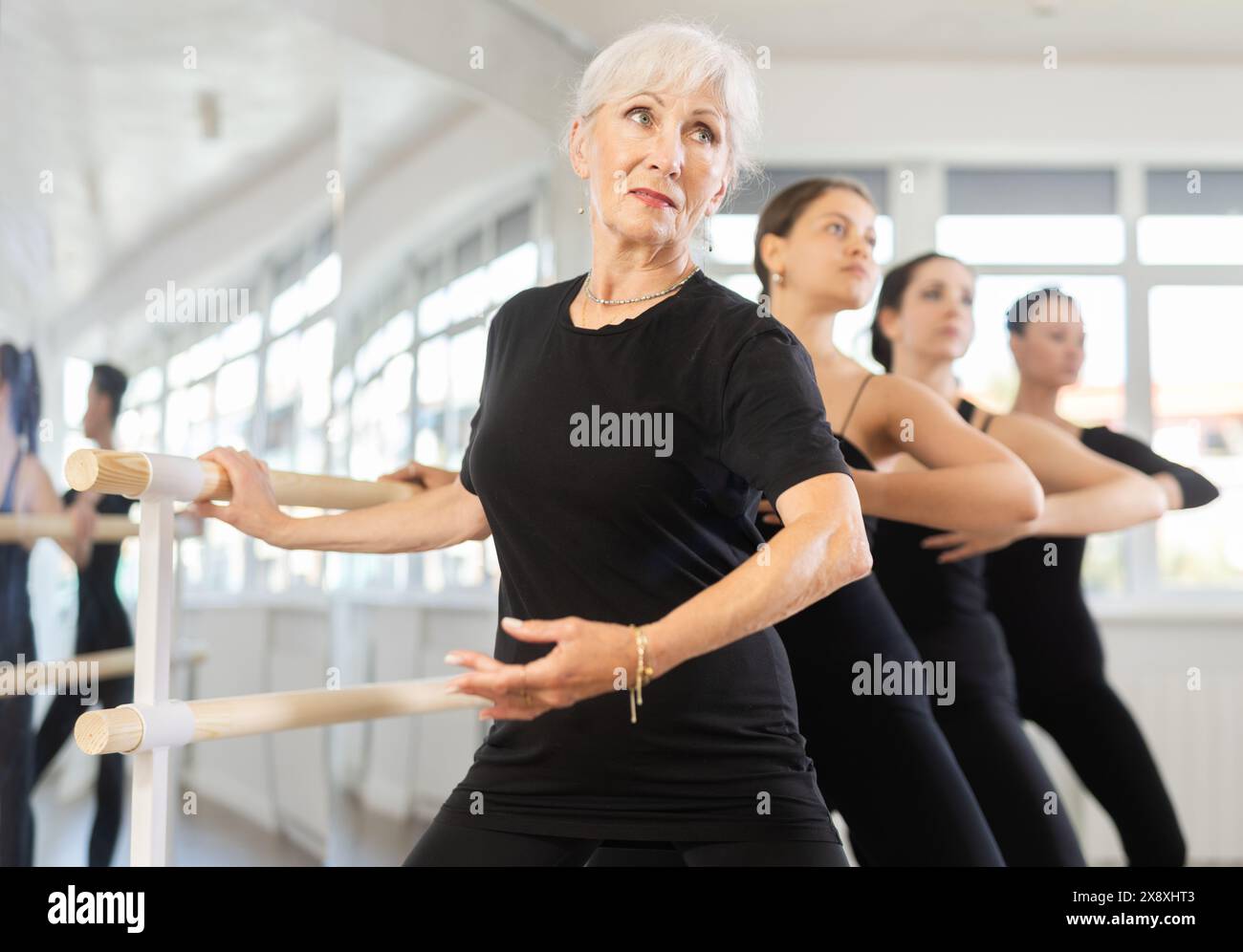 Female ballet dancers doing various ballet movements at ballet barre in ...