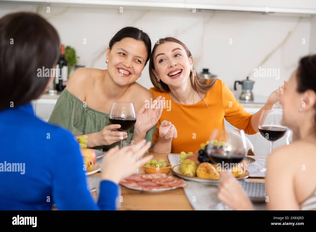 Girlfriends drinking wine and having conversation over dinner at house ...