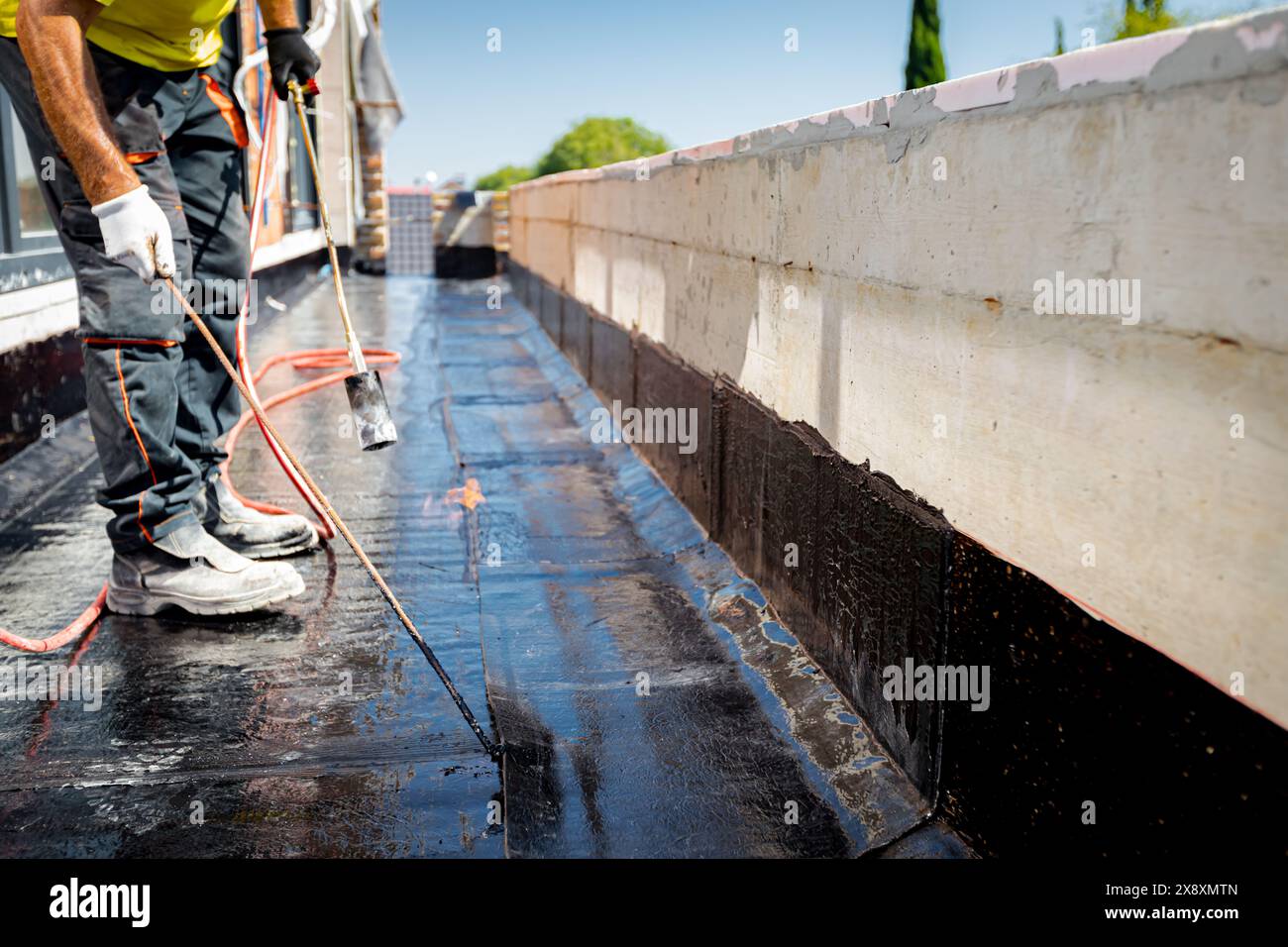 Worker is heating, melting bitumen waterproofing installation over concrete using propane ...