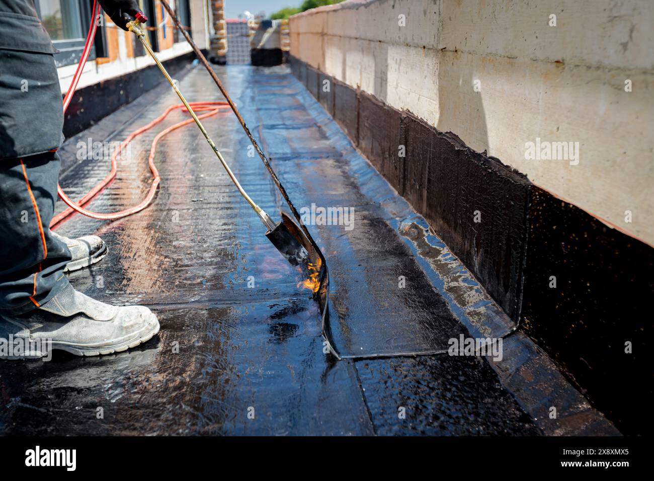 Worker is heating, melting bitumen waterproofing installation over concrete using propane ...