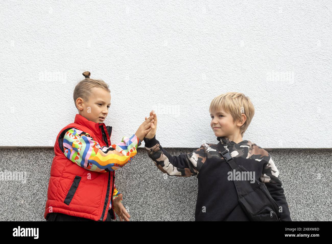 Two 7-year-old boys joyfully greet each other with their hands. concept ...