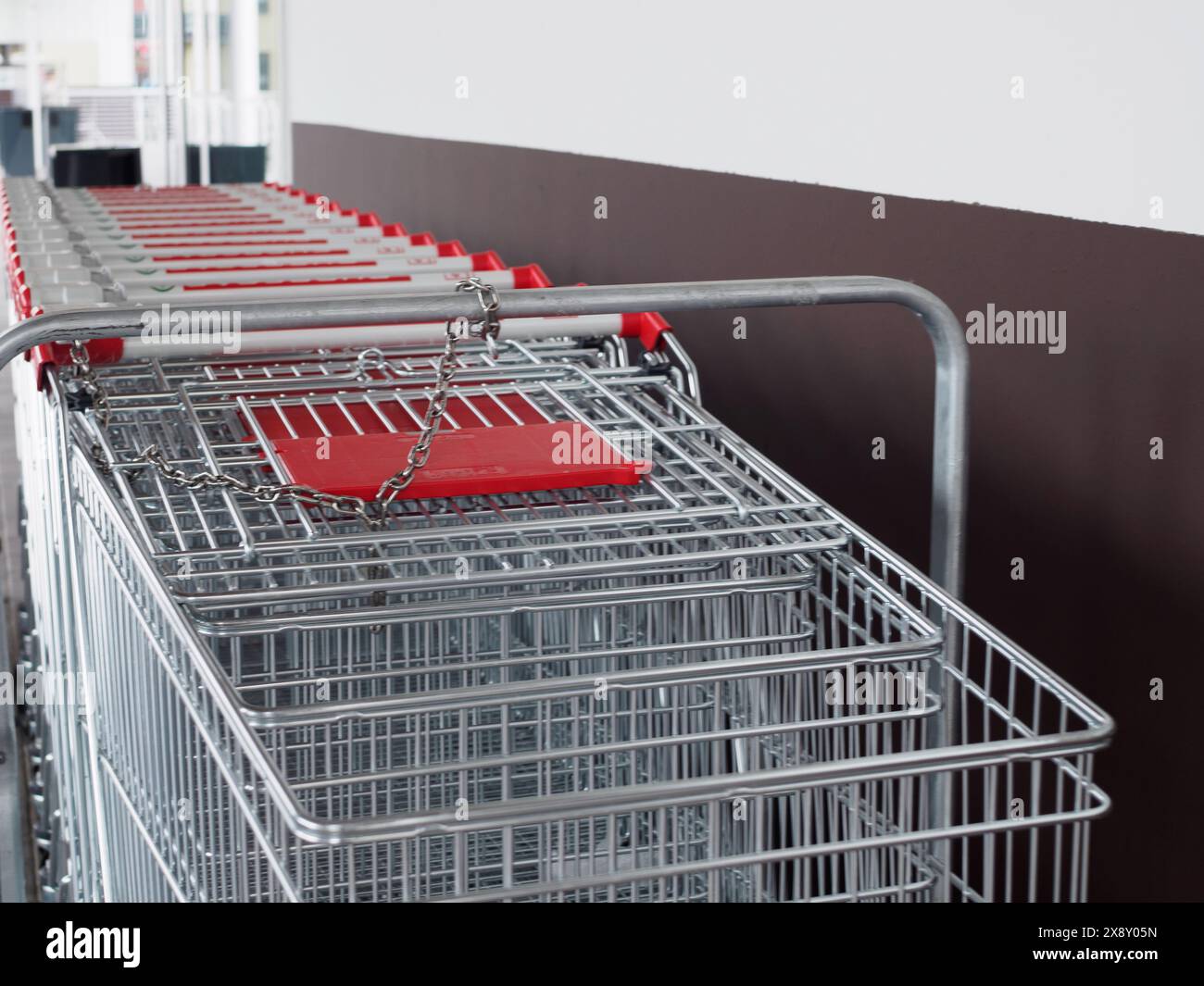 Row of metallic shopping carts with red handles neatly arranged inside ...