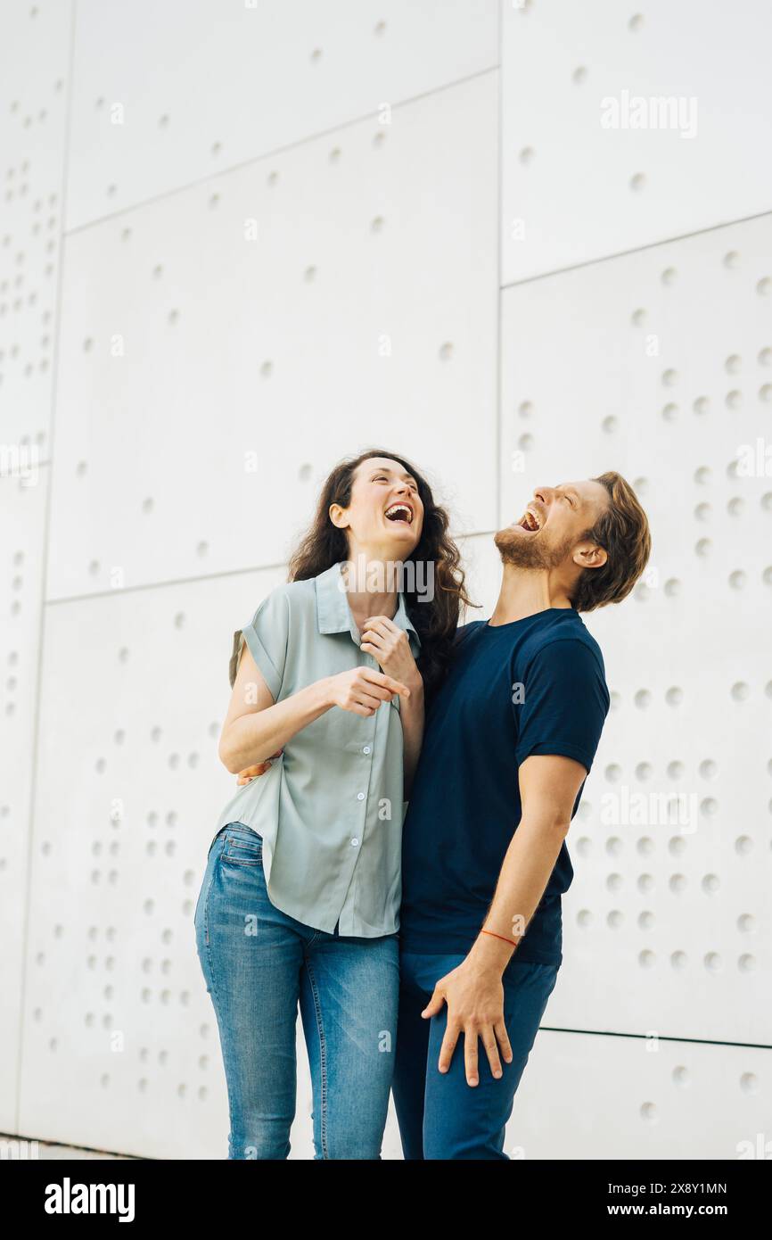 Couple laughing together while standing against a modern white wall ...