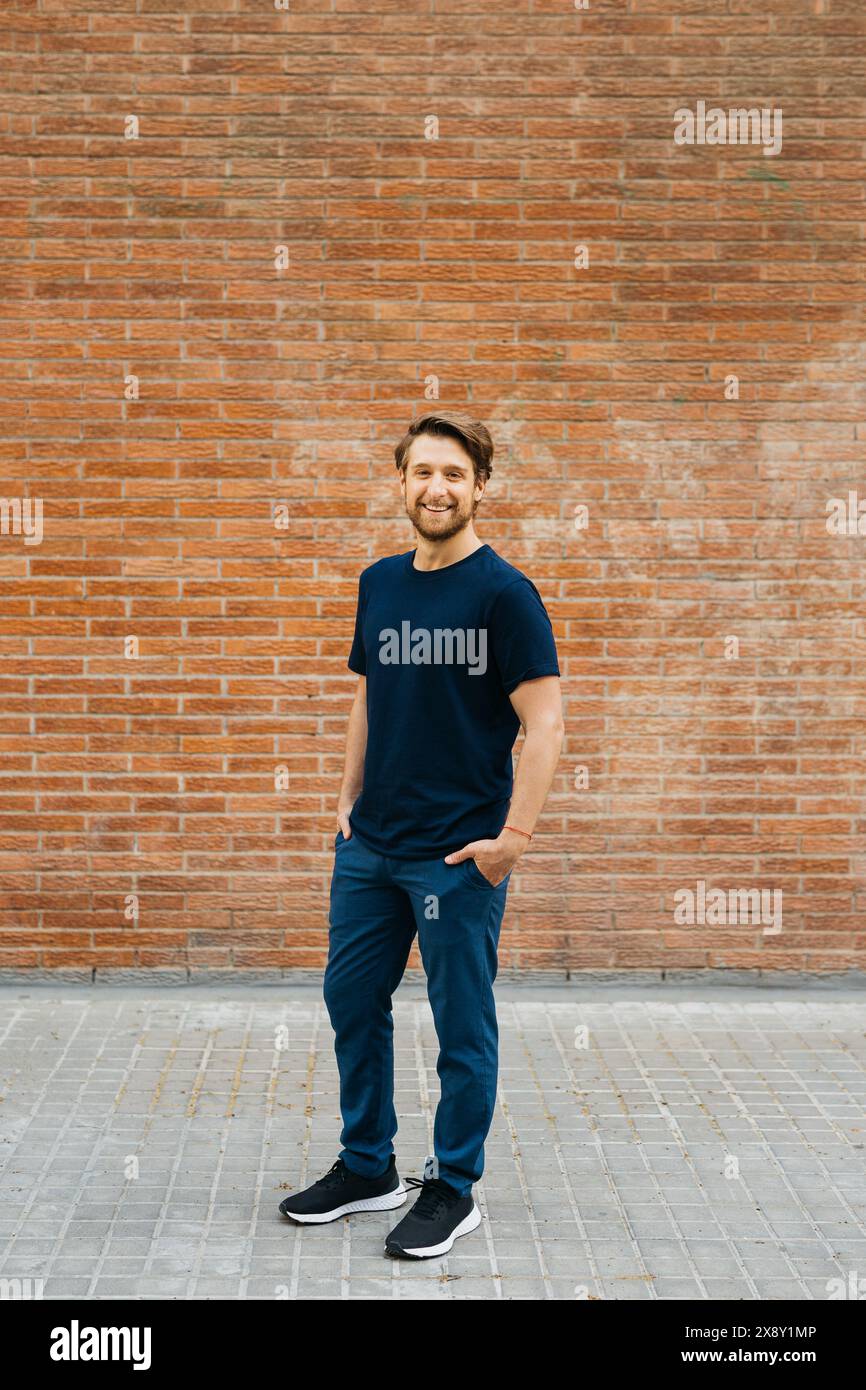 Portrait of a young man standing against a brick wall, smiling ...