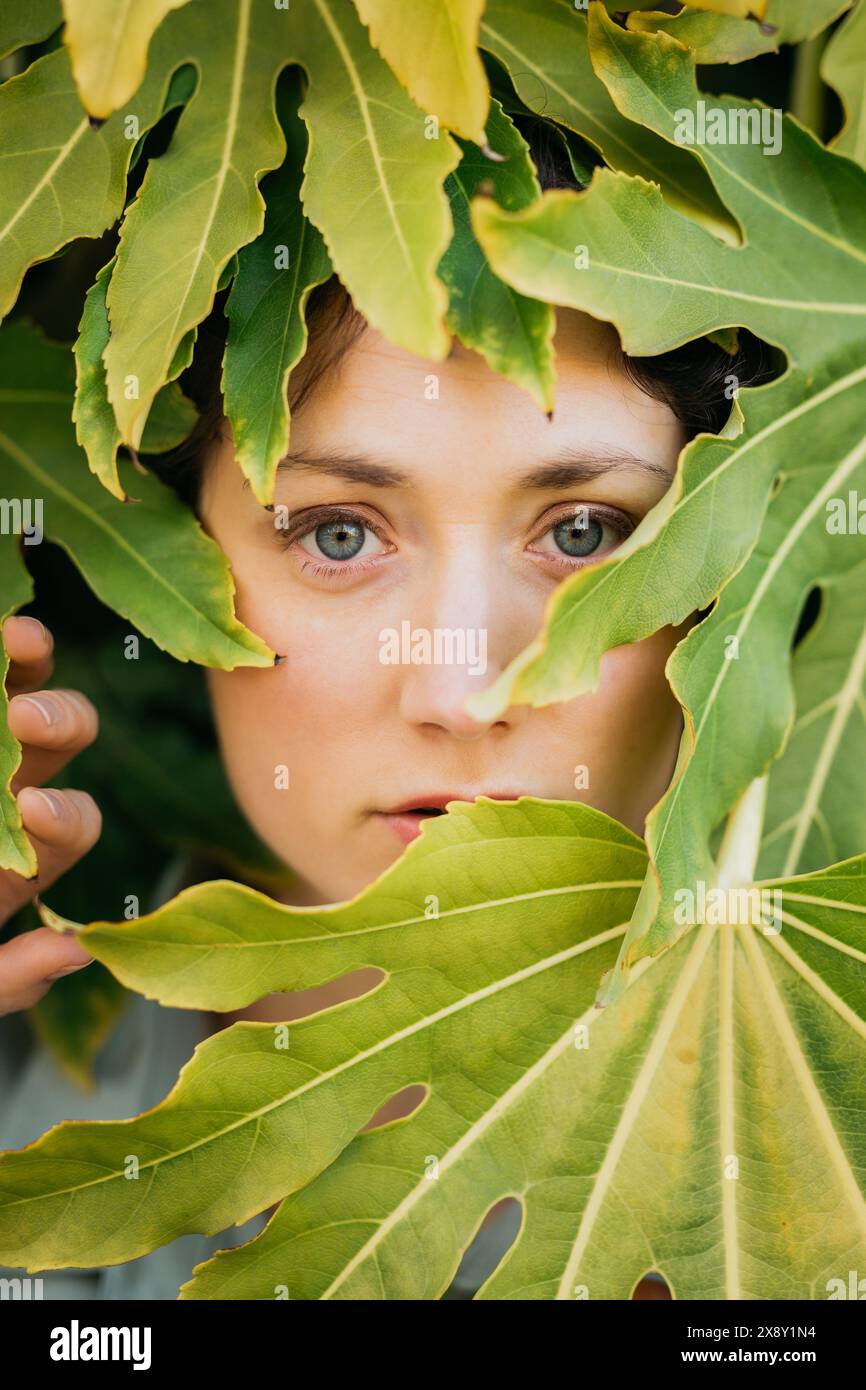 A woman peers through large green leaves, her face framed by the ...