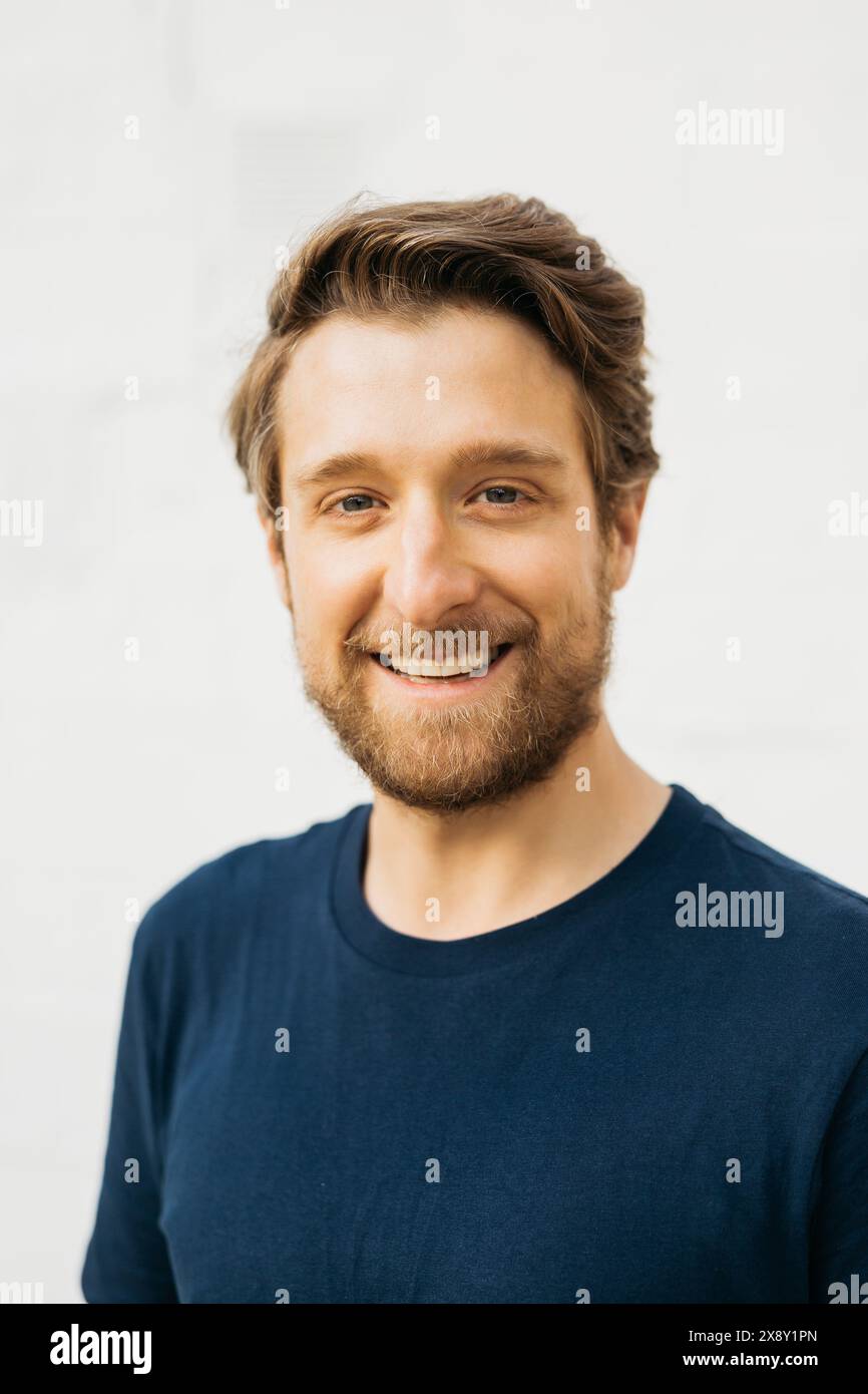 Portrait Of A Cheerful Man Standing Against A White Wall Wearing A