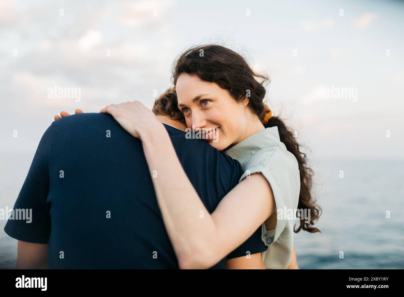 Couple embracing by the sea, with the woman smiling gently as she holds ...