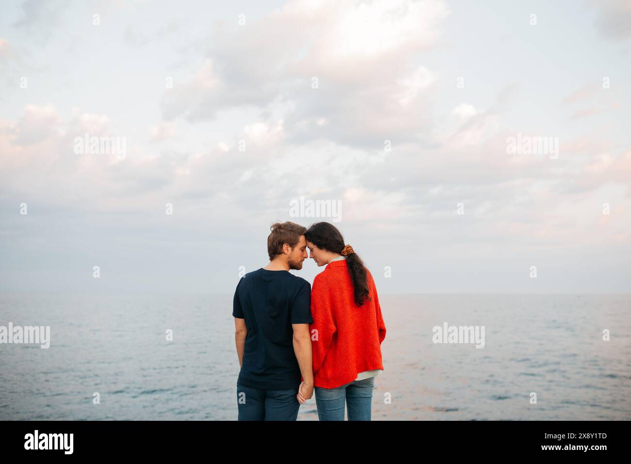 Couple standing at the edge of the sea, holding hands and touching ...