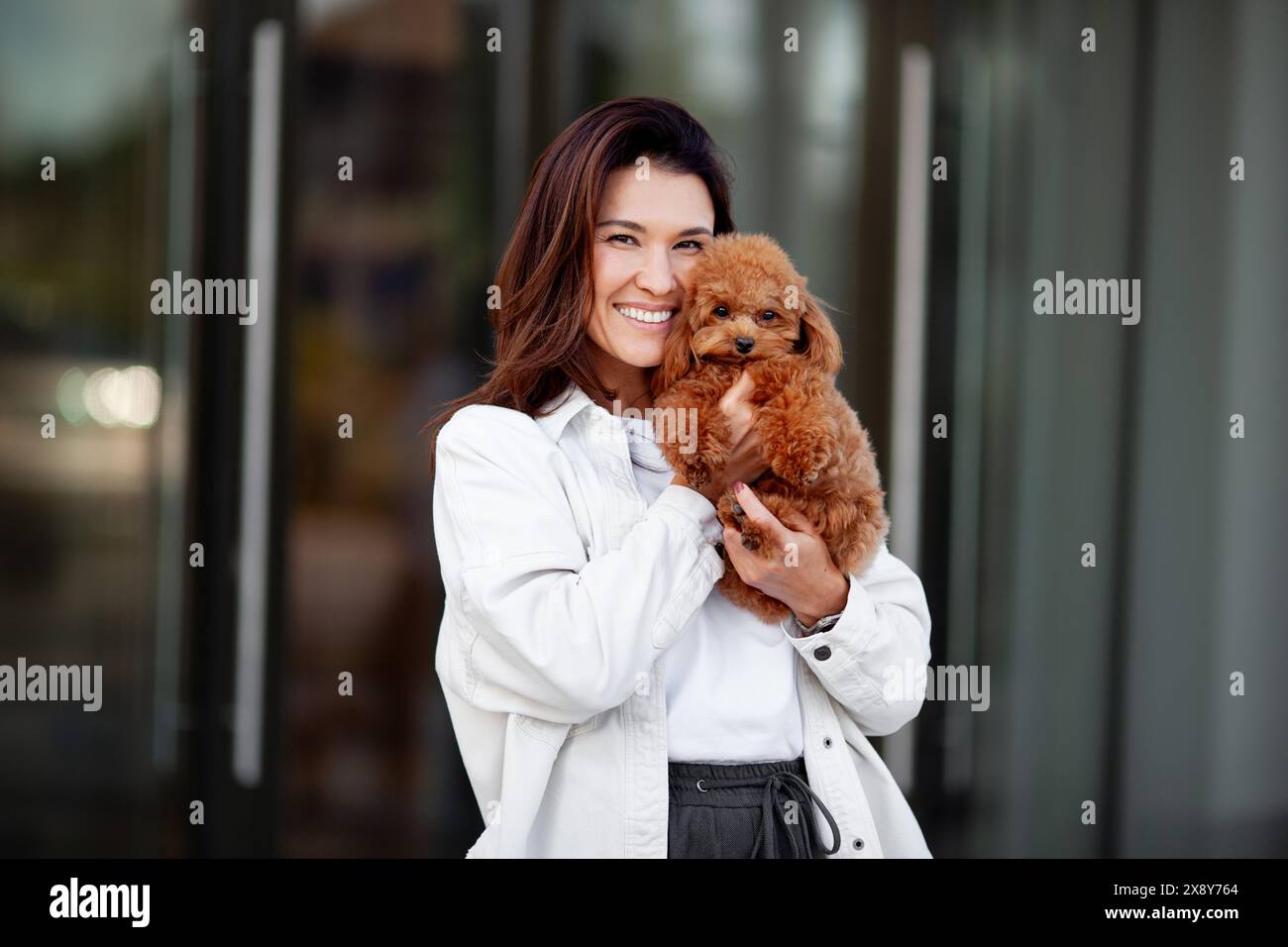 Beautiful happy dark haired woman holds and hugs small dog poodle ...