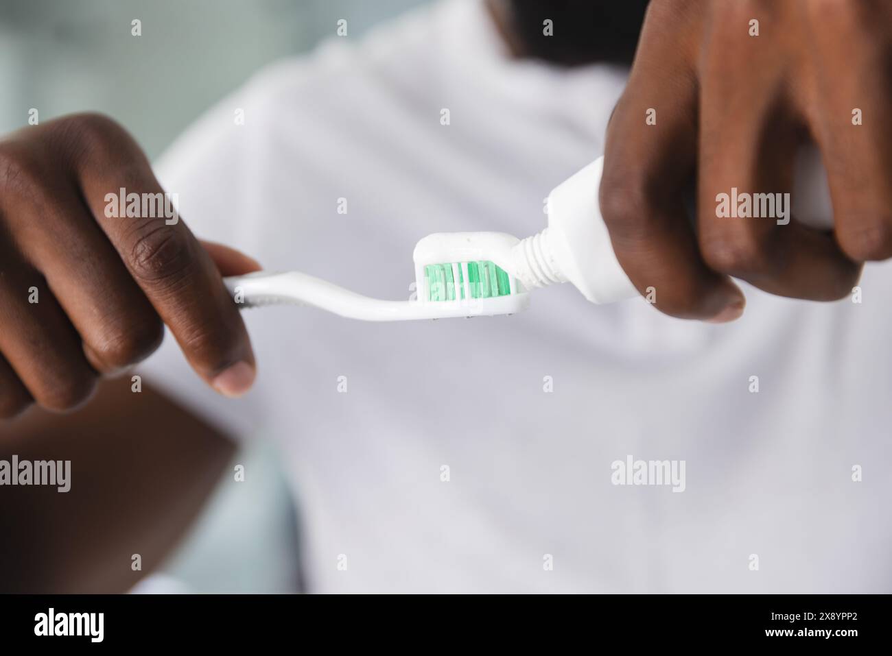 At home, African American man applying toothpaste on toothbrush. Wearing a white shirt ...