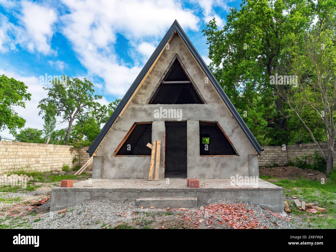 A small house with a brick wall and roof is being built. The roof has a ...