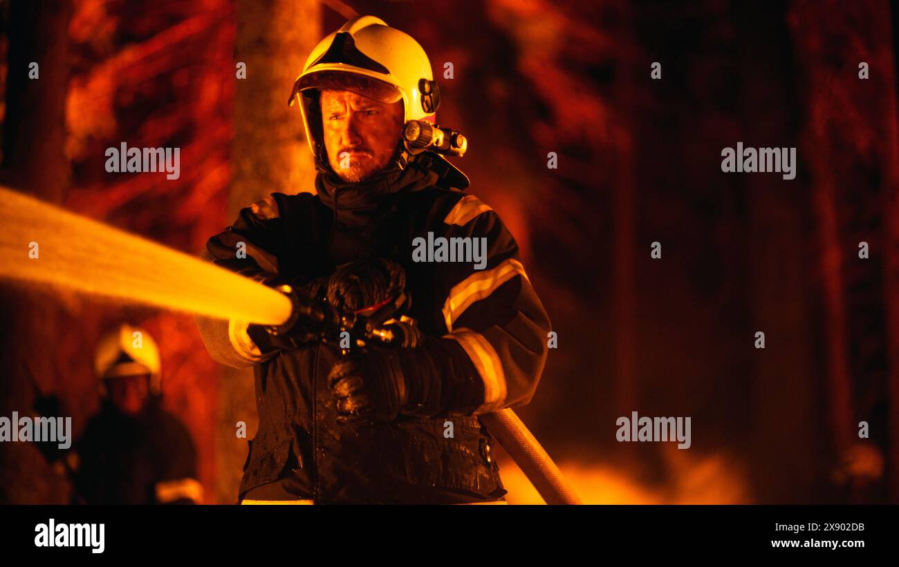 Focused Brave Professional Firefighter Using a Firehose to Fight a ...