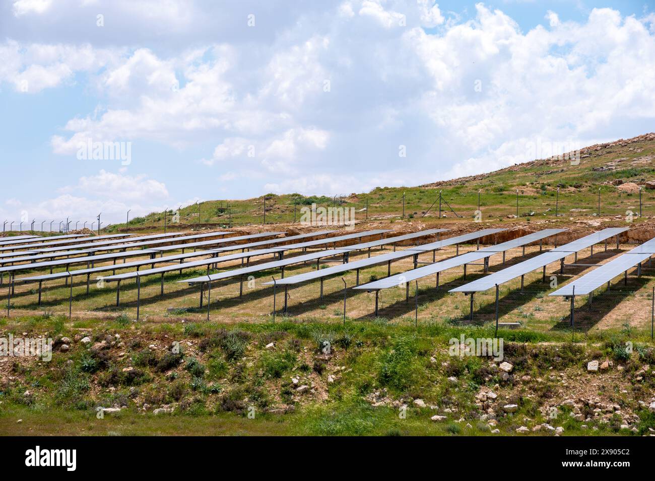 A solar farm is built on a hill under a cloudy sky, surrounded by ...