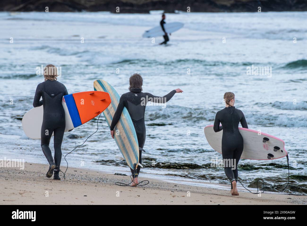 Three surfers carrying their surfboards walking along the shoreline on ...