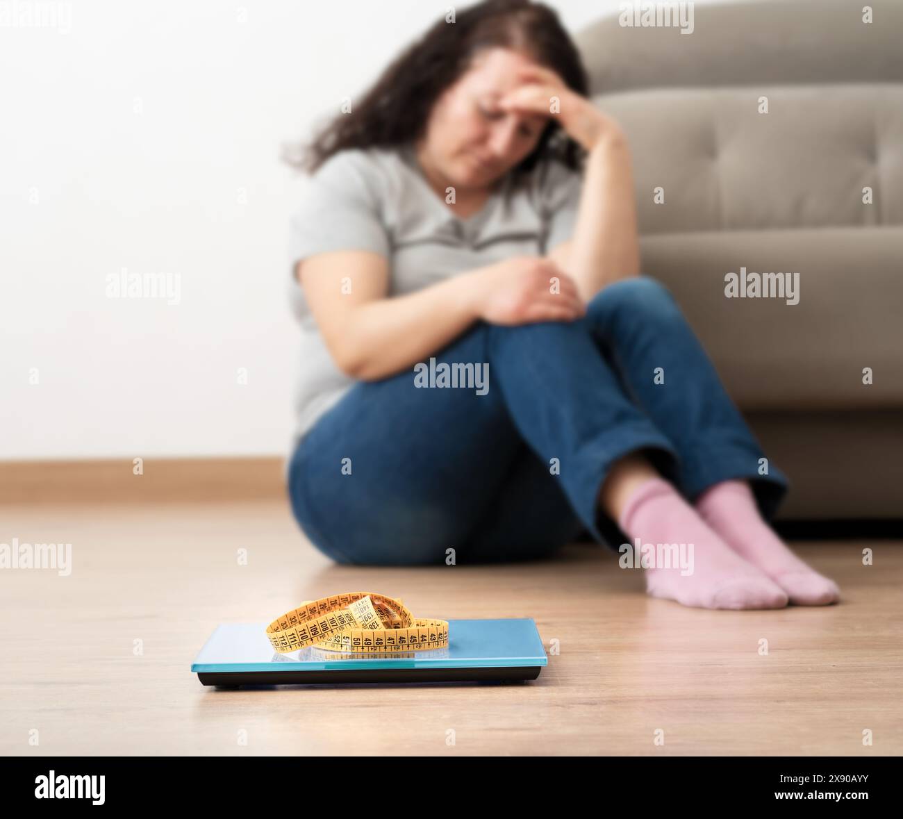 Sad woman complaining about her body weight sitting on the floor with a ...