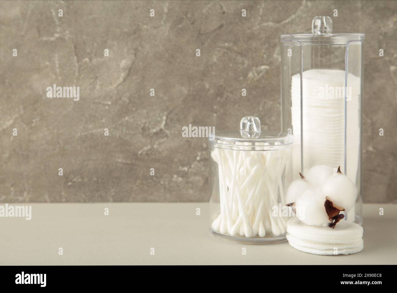 Cotton pads and cotton sticks in containers with cotton flower on grey ...