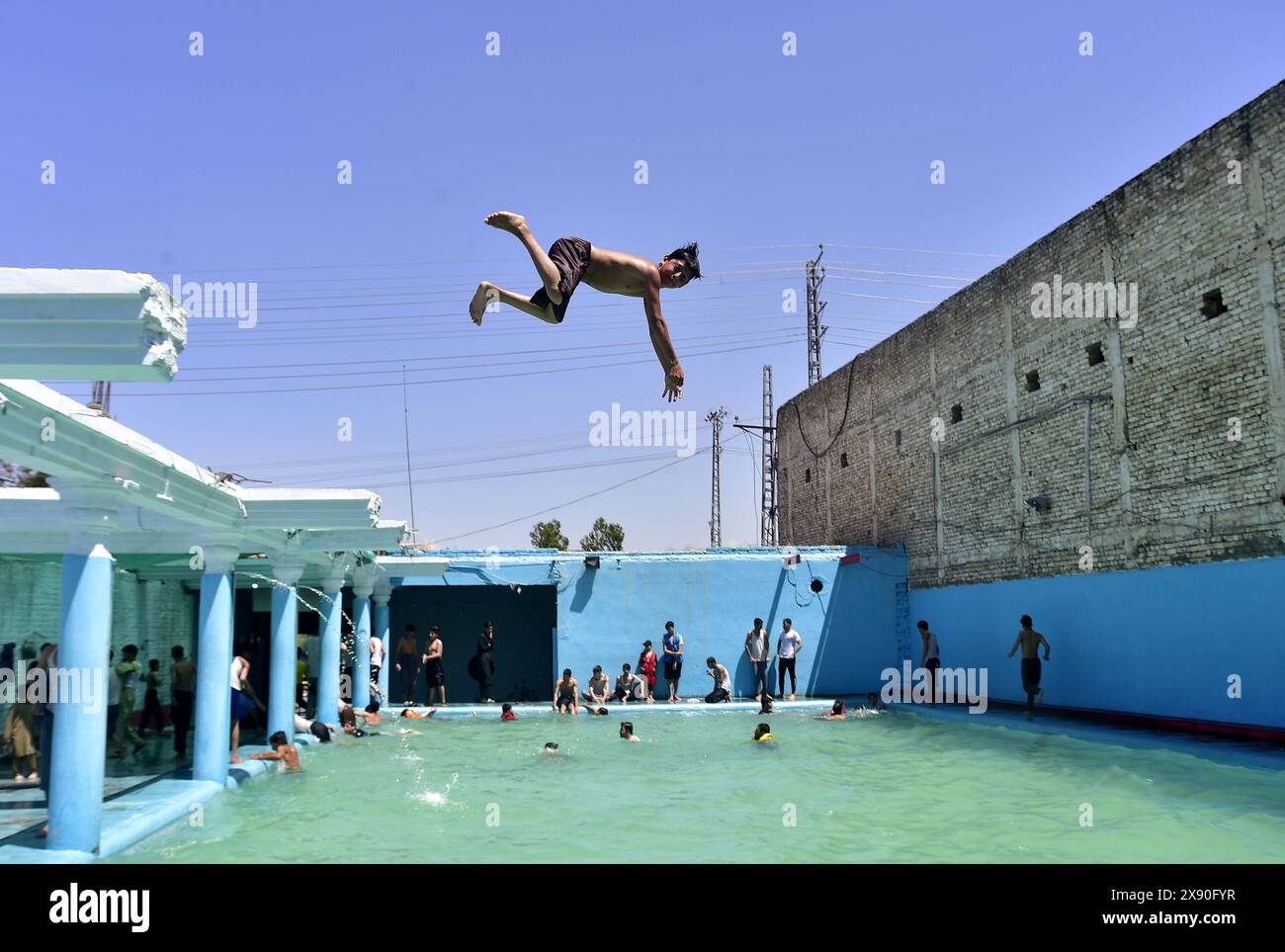 Peshawar, Pakistan. 28th May, 2024. A boy jumps into a swimming pool to ...