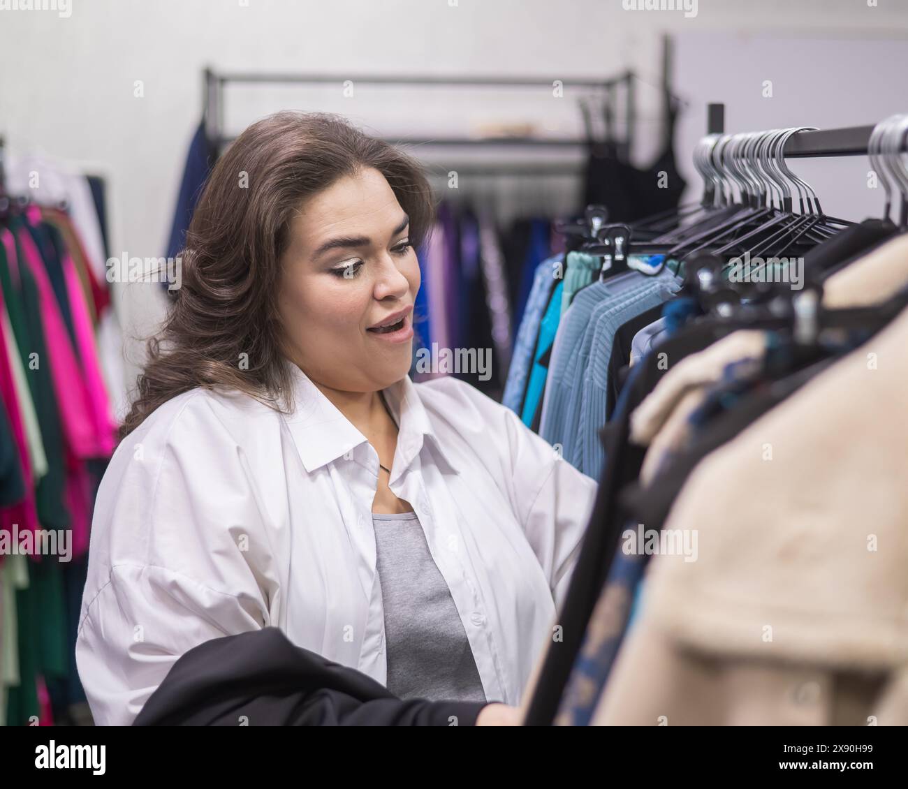 A fat woman in a plus size store chooses clothes while sorting through ...
