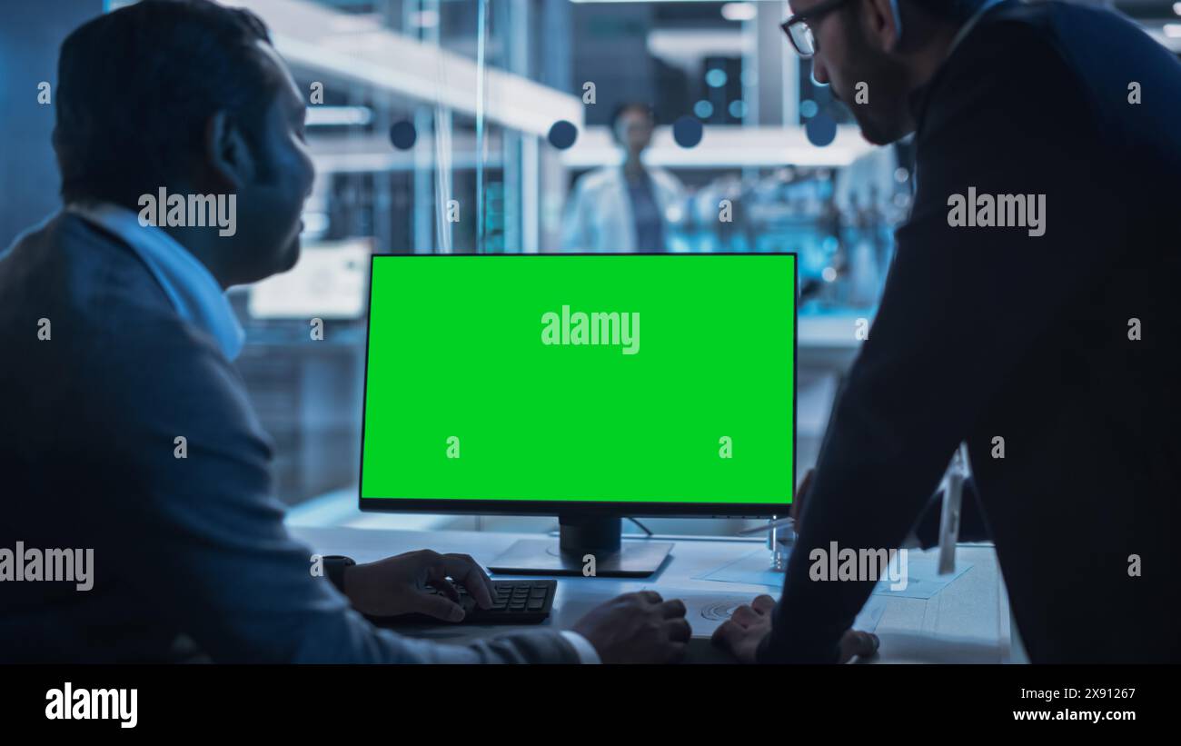 Two Developers Working on Computer with Green Screen Mock Up Display. Scientific Lab ...