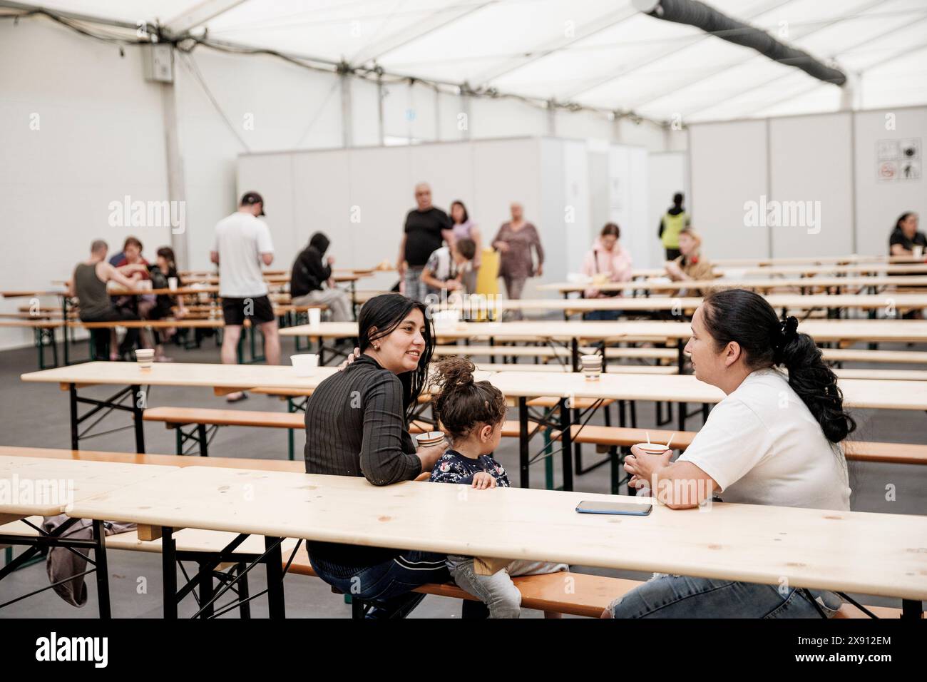 28 May 2024, Berlin: Refugees sit at tables in the large common room in ...