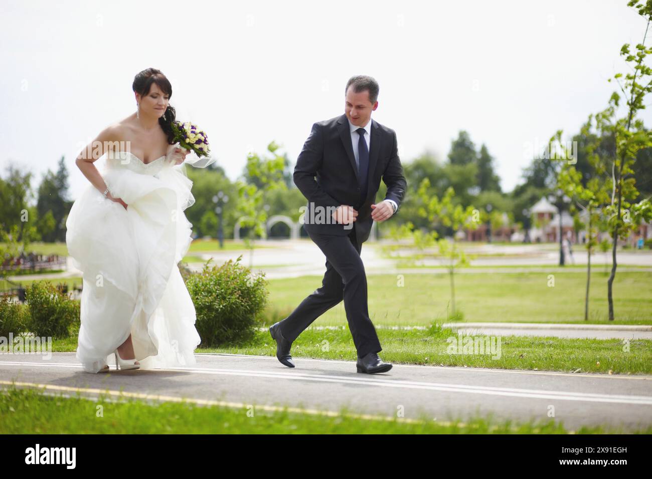 A bride and groom walking on a path outdoors surrounded by greenery ...