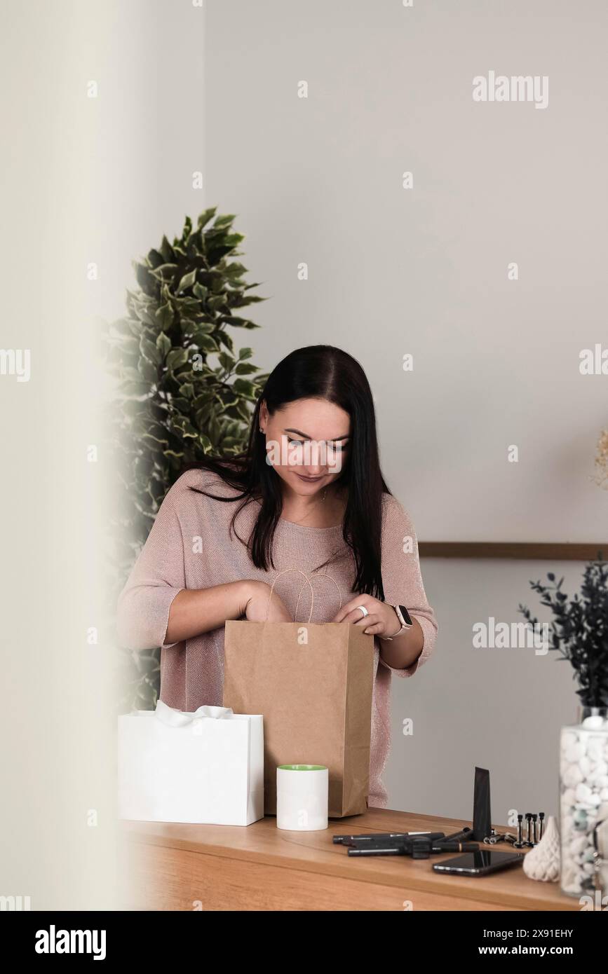A woman is unpacking a paper bag at a wooden desk with various items ...
