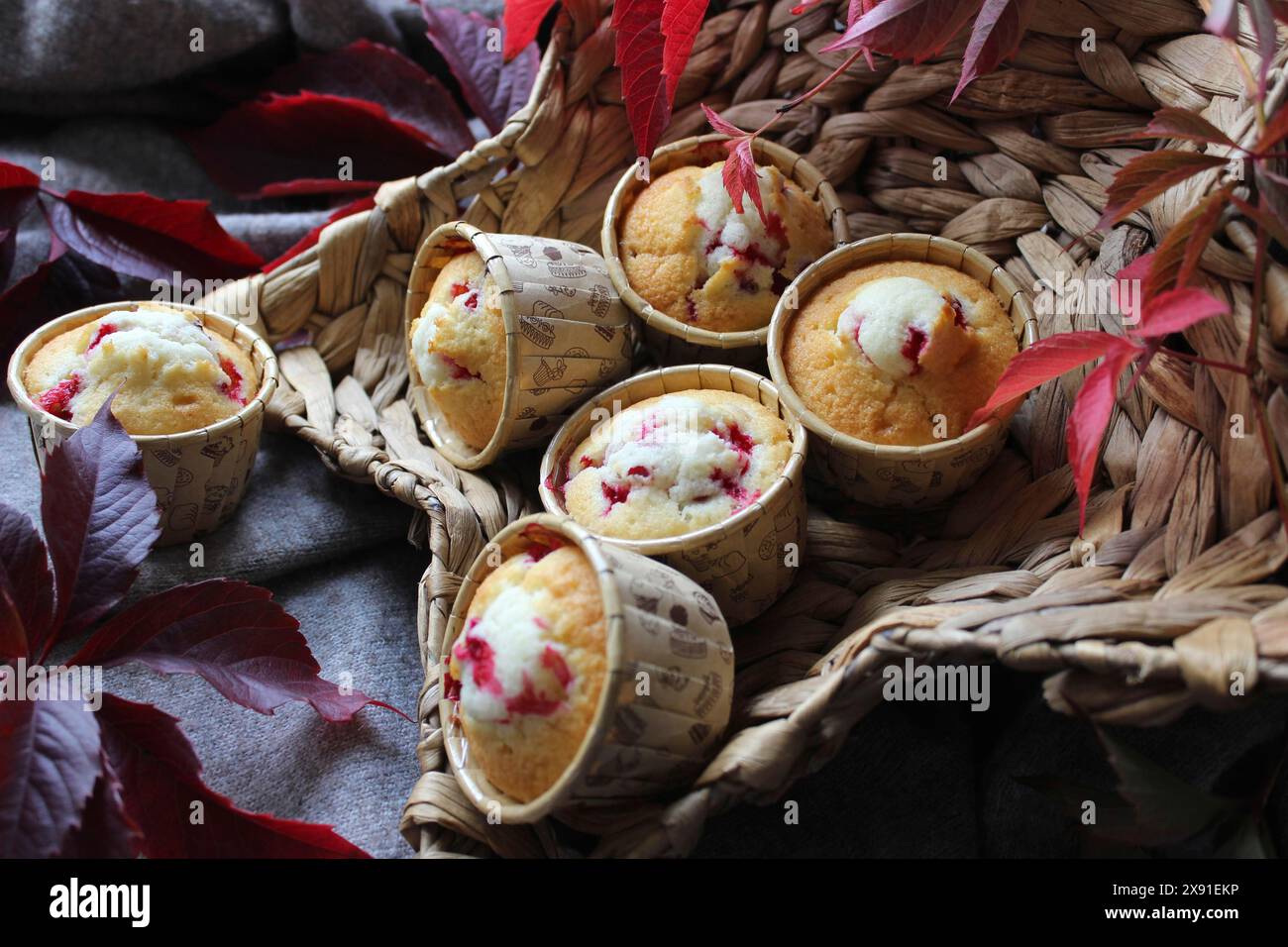 Six homemade muffins in decorative cups on a woven basket surrounded by ...