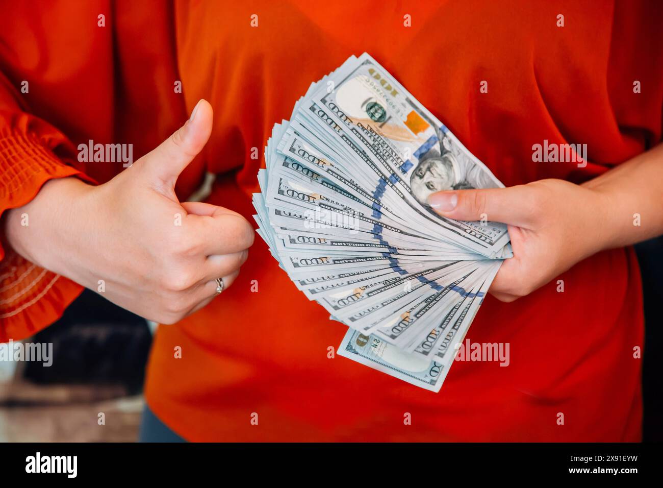 Person holding a fan of hundred dollar bills and showing a thumbs-up ...