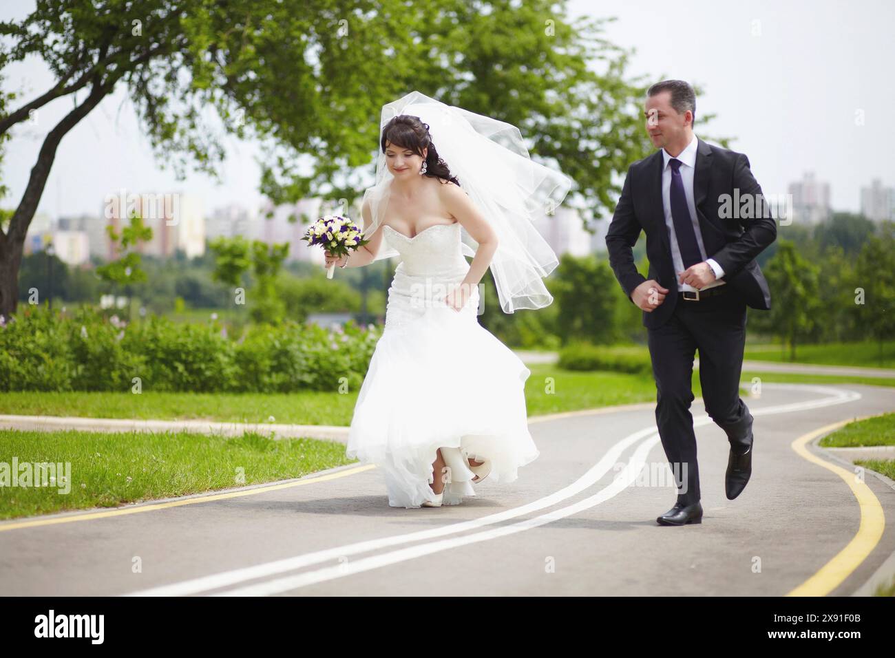 Bride and groom running down a path in a park, both laughing and happy ...