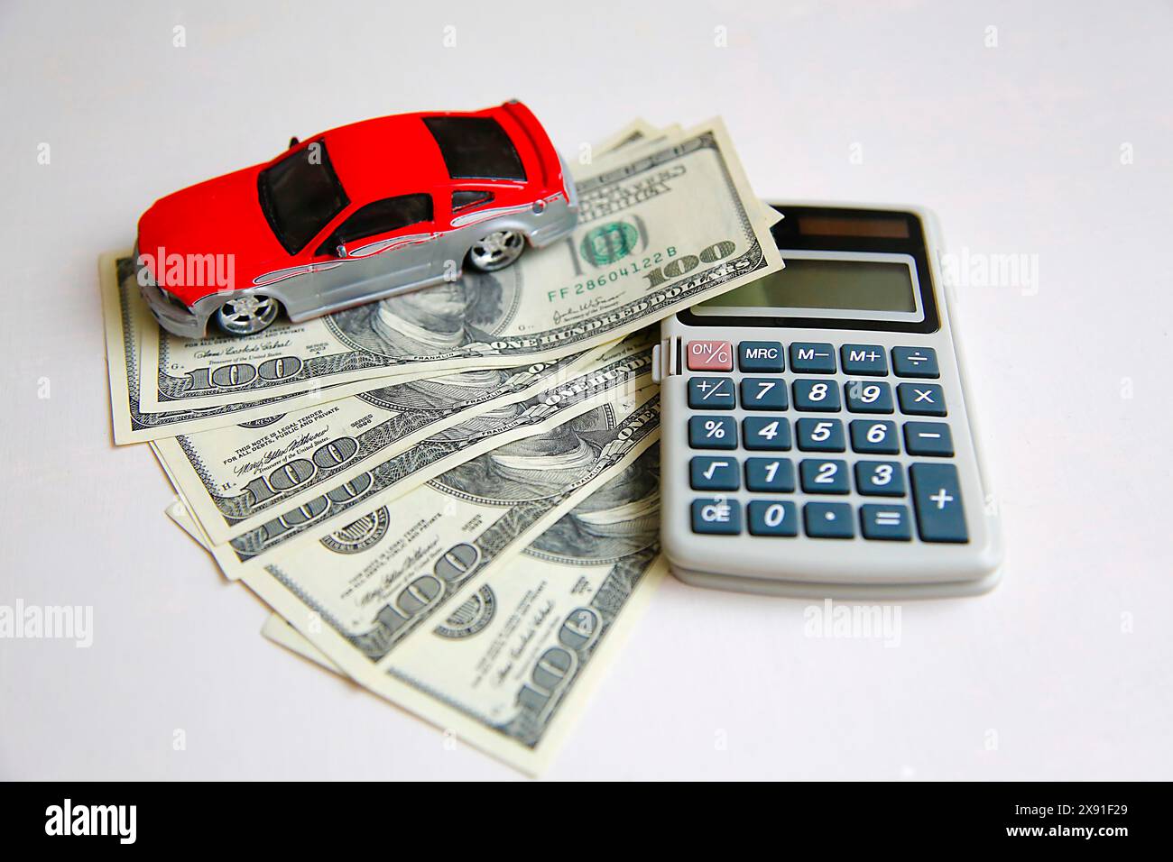 A toy car placed on dollar bills next to a calculator, symbolizing ...