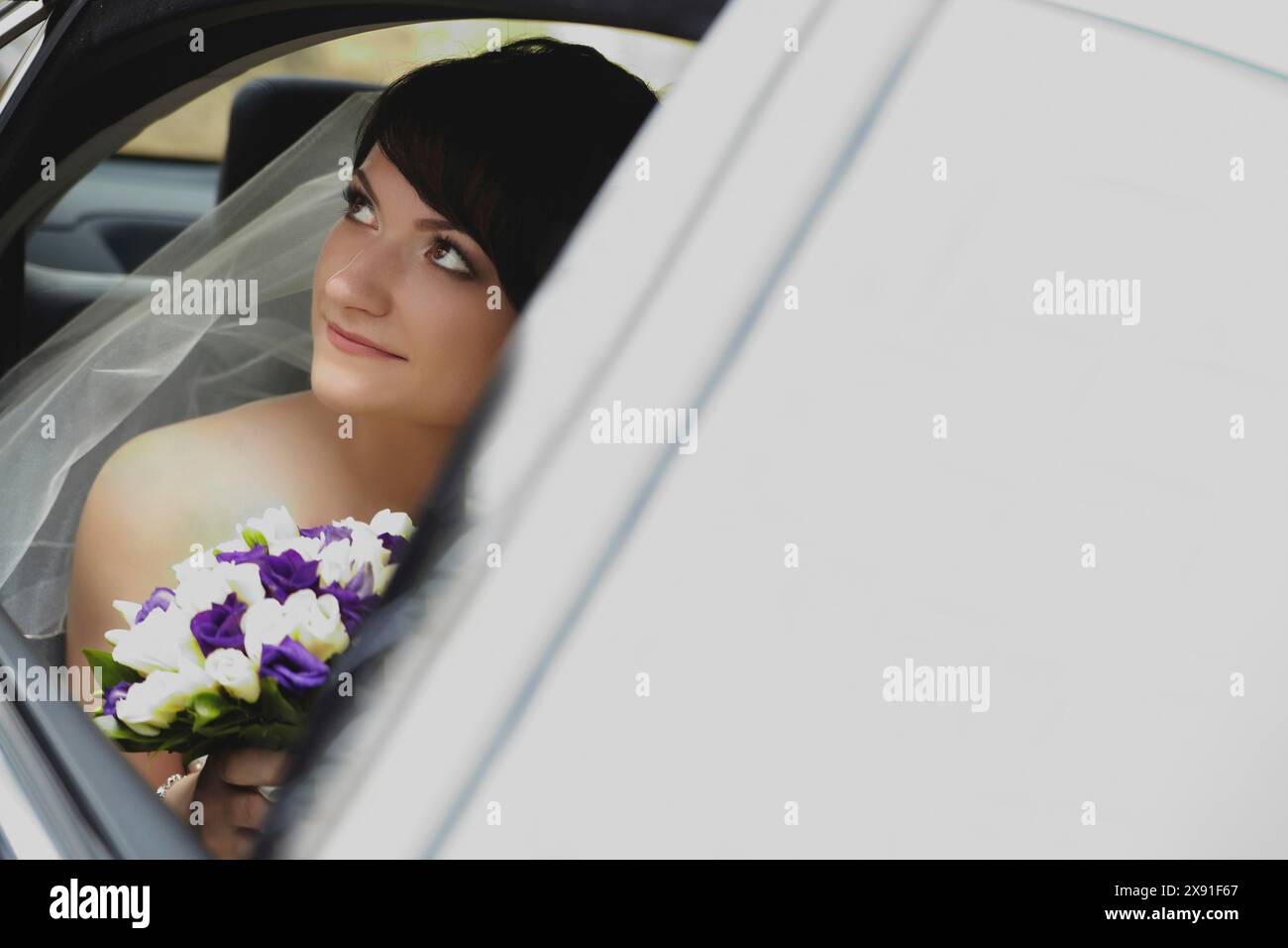 Bride in a car looking out the window with a smile, holding a bouquet ...