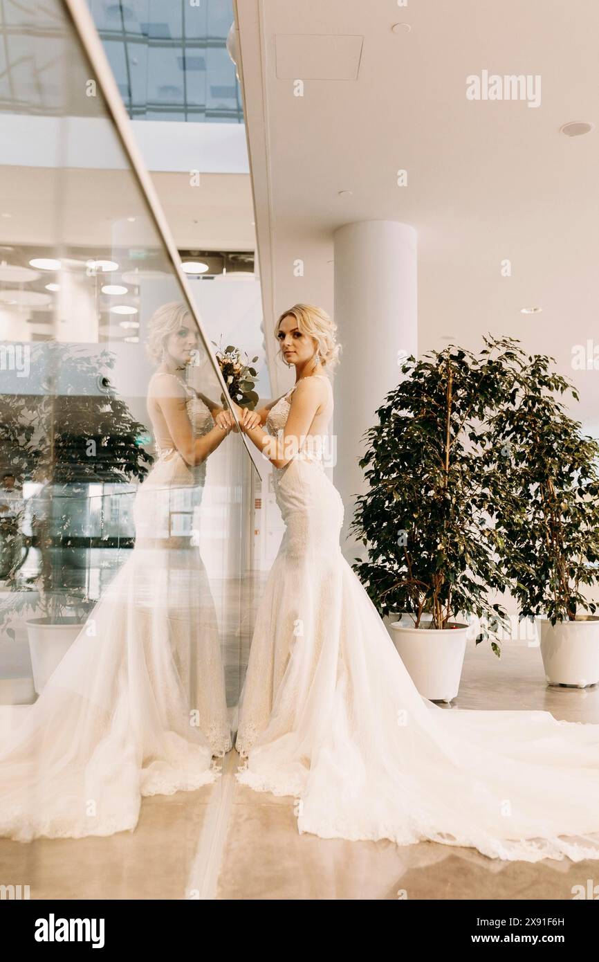 Bride in an elegant wedding dress stands indoors, her reflection ...