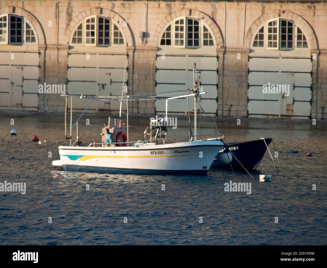 A boat in the harbour in front of a building with stone walls and many ...