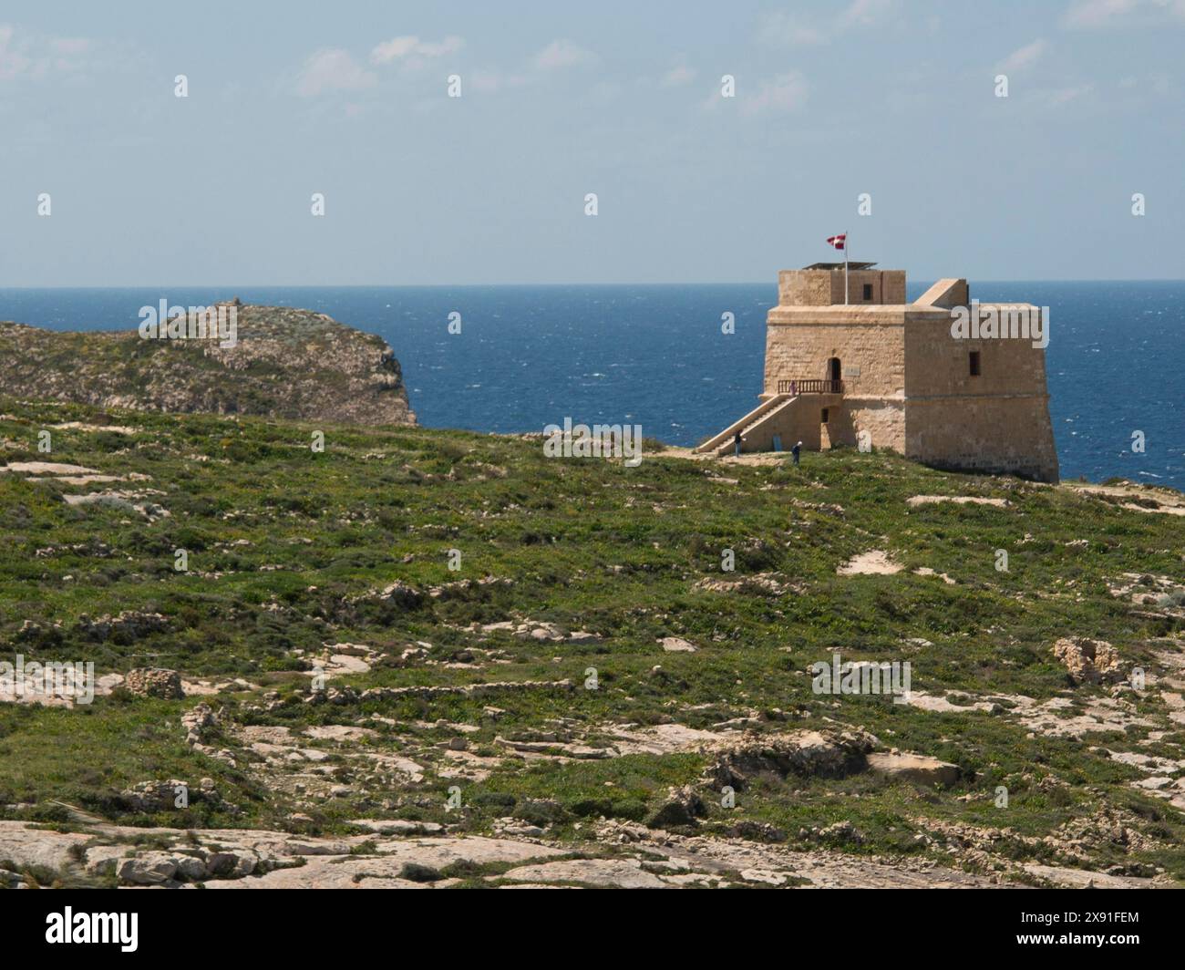Historic watchtower on a green, rocky coastal area under a blue sky ...