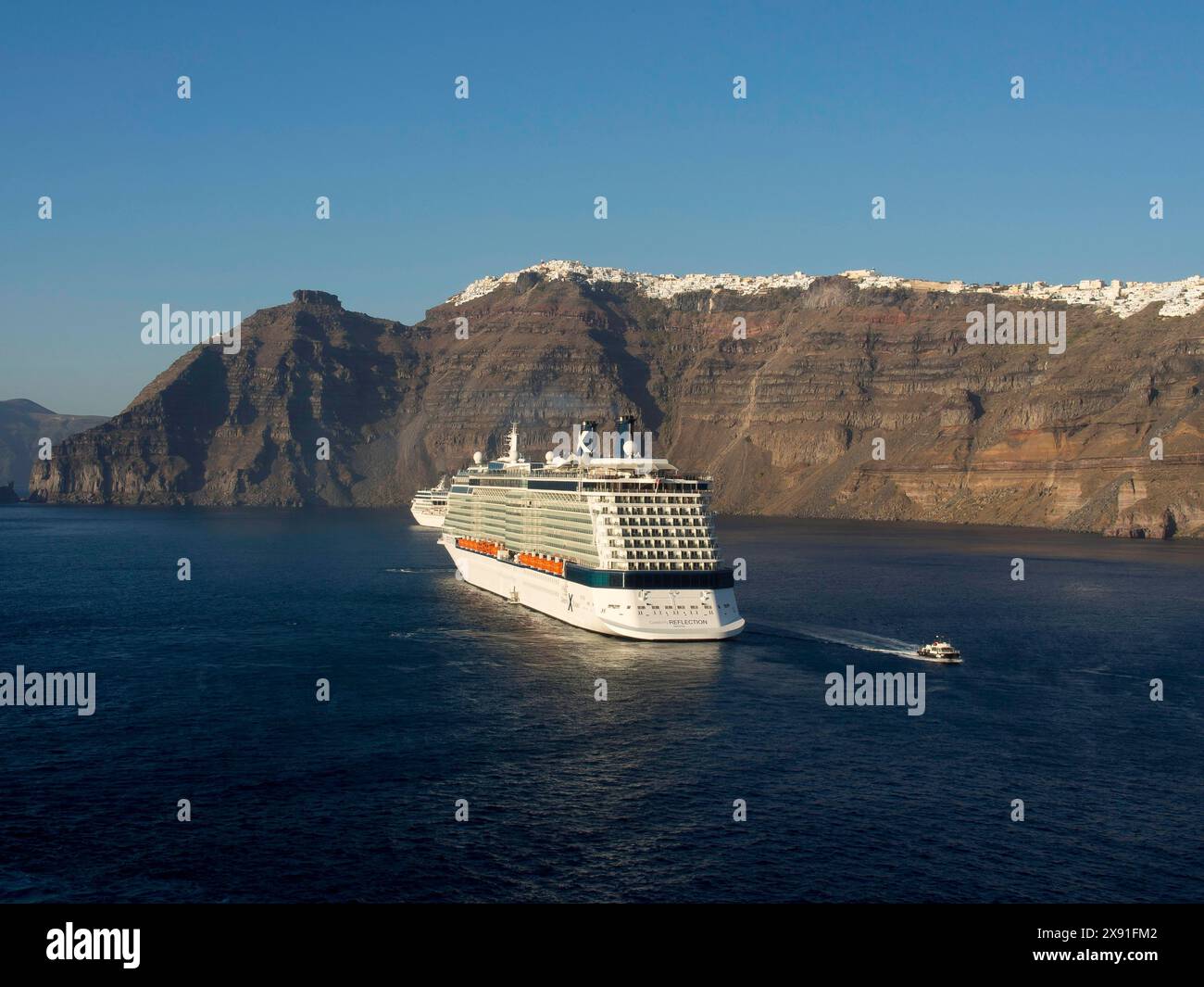 Two cruise ships and a boat in blue water near steep cliffs, brown ...