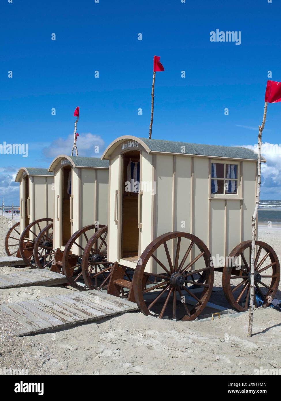 Three beige changing cabins with large wooden wheels on a beach under a ...