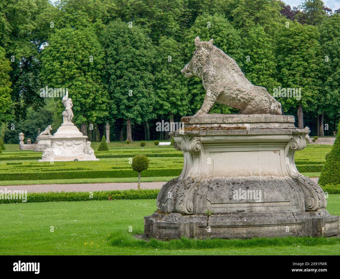 Stone sculpture of a boar in a spacious park with hedges and trees ...