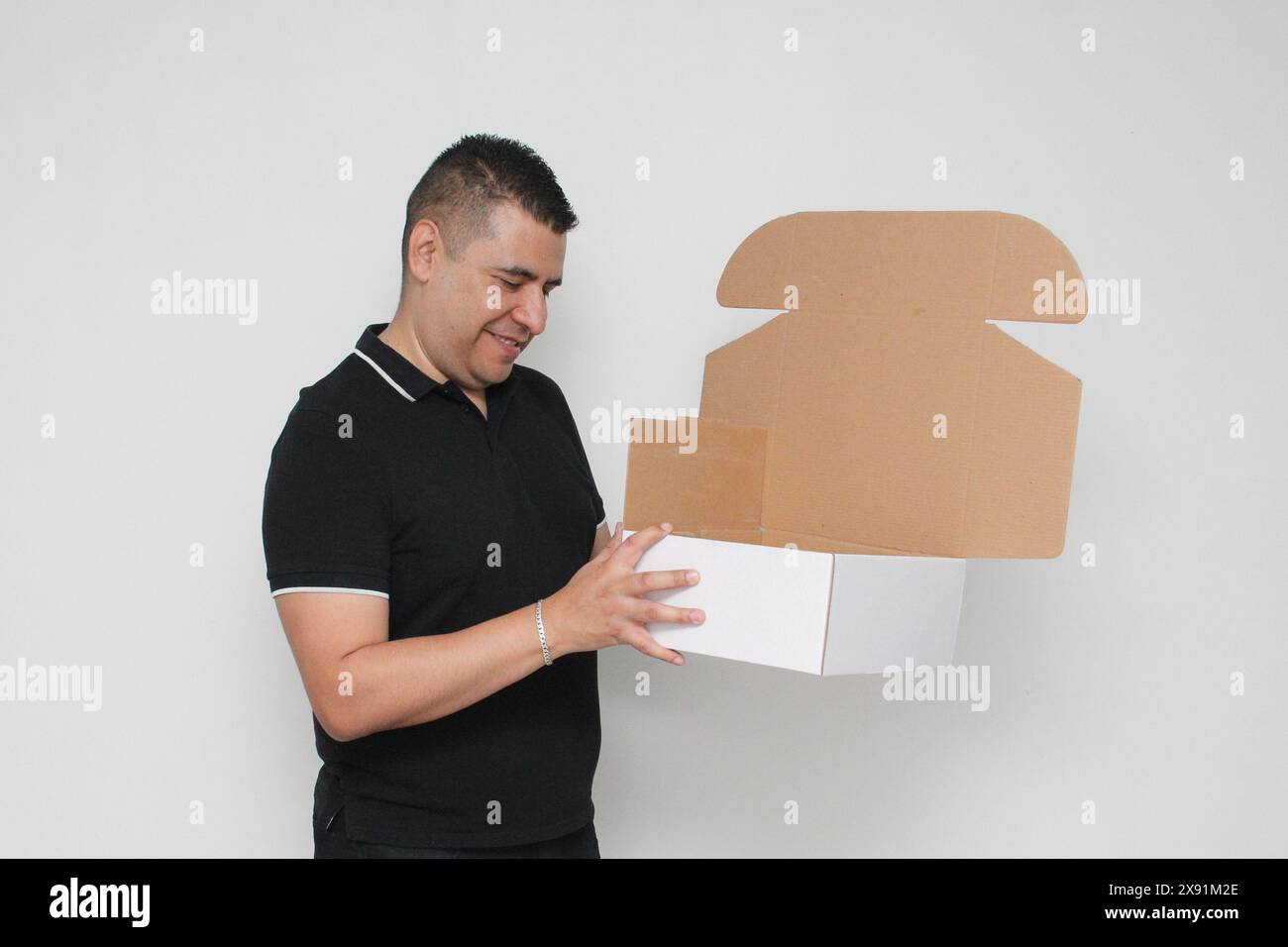 Latino adult man assembles a cardboard box following the instructions ...