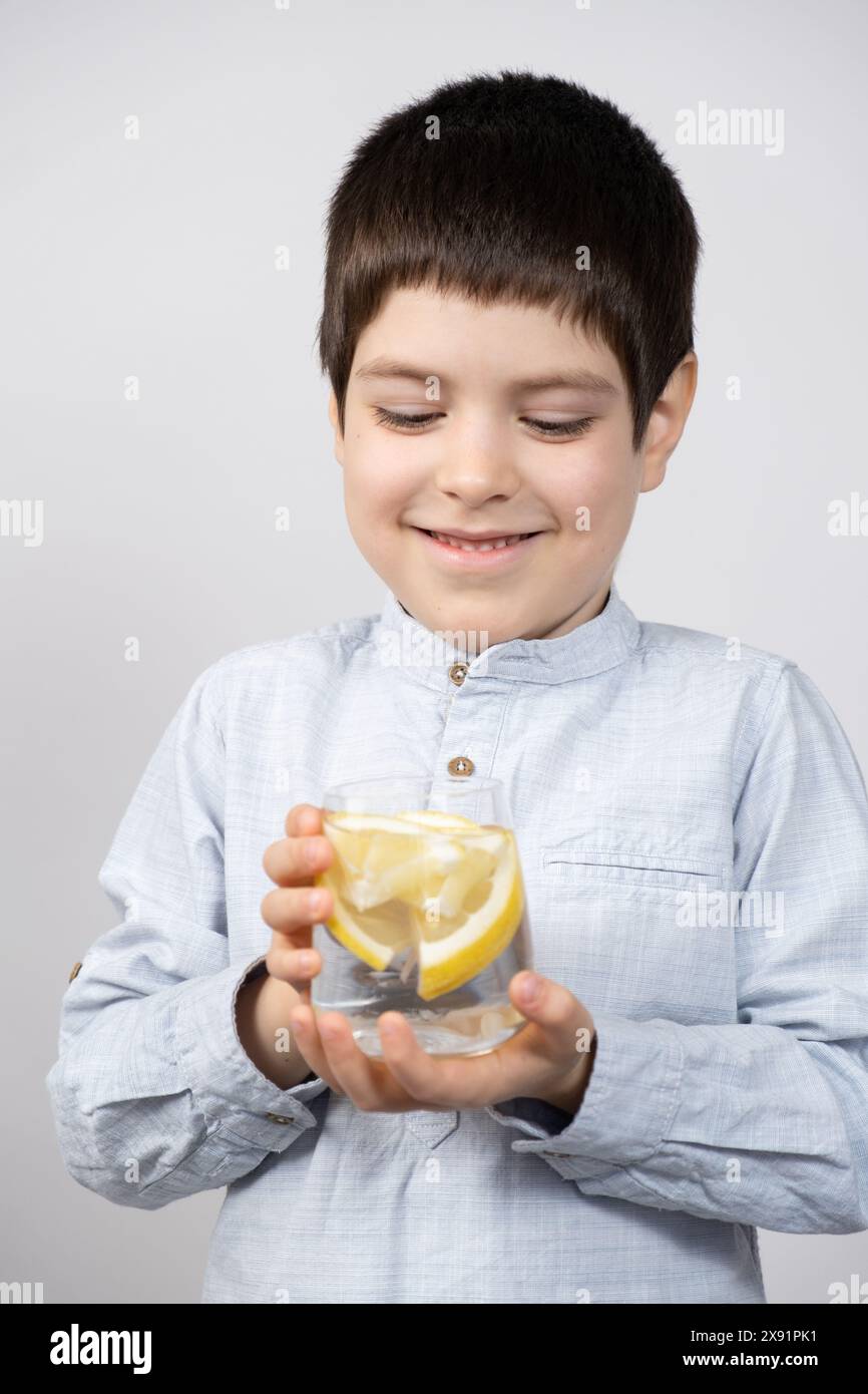 Happy six-year-old boy holding a glass of lemon water in his hands ...