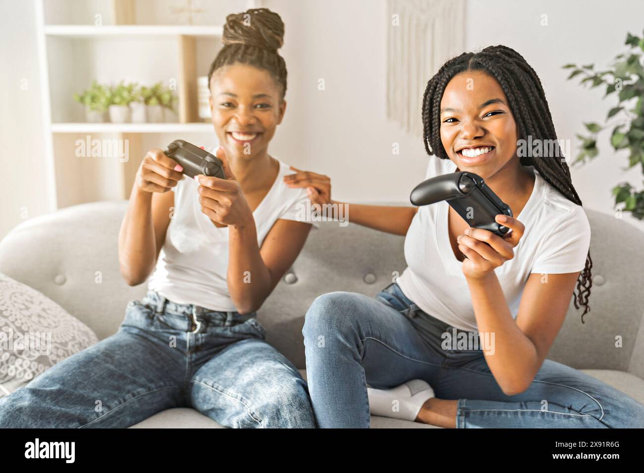 Mother and daughter sitting on sofa at home play video game together ...
