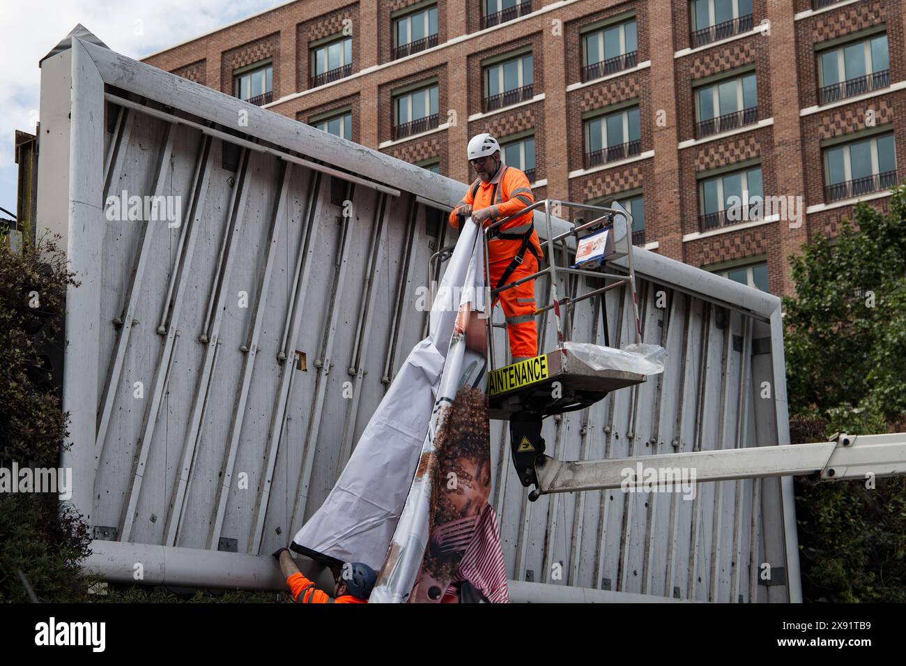 Workers in high visibility vests on an elevated platform installing a large outdoor billboard ...
