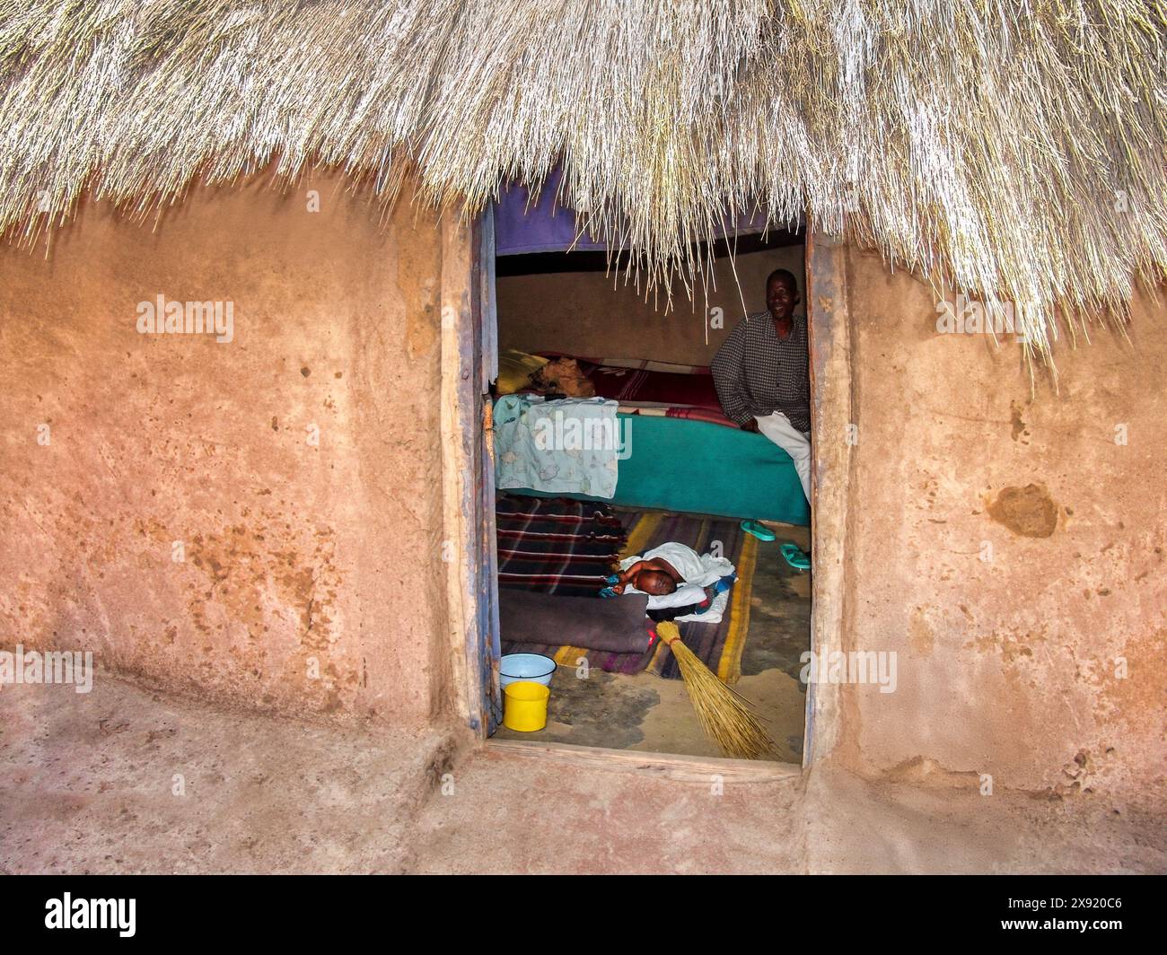 african mud house with thatched roof; man with baby inside of a shack ...