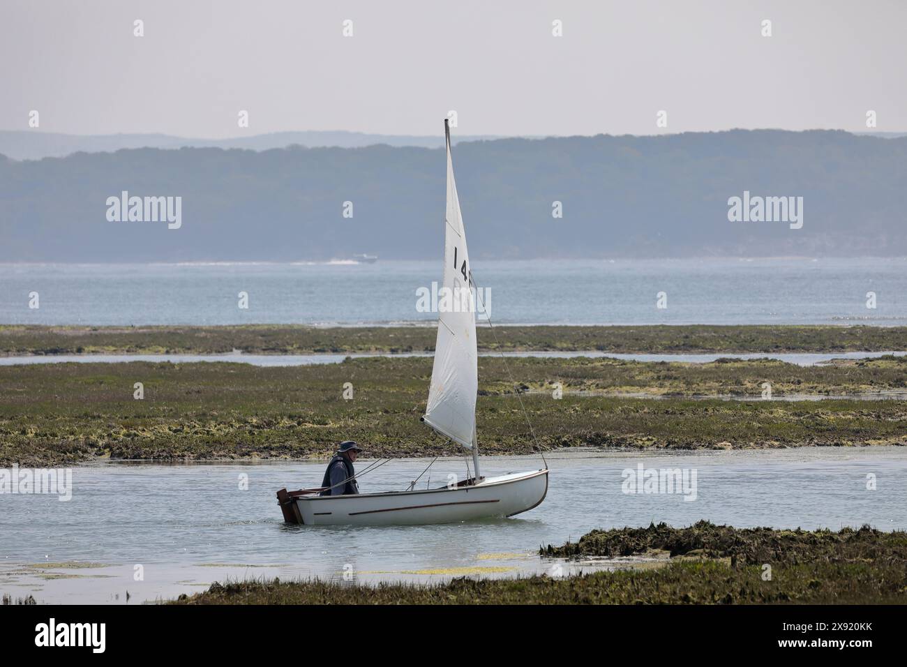 A small sailing boat with a white sail travelling from left to right on ...