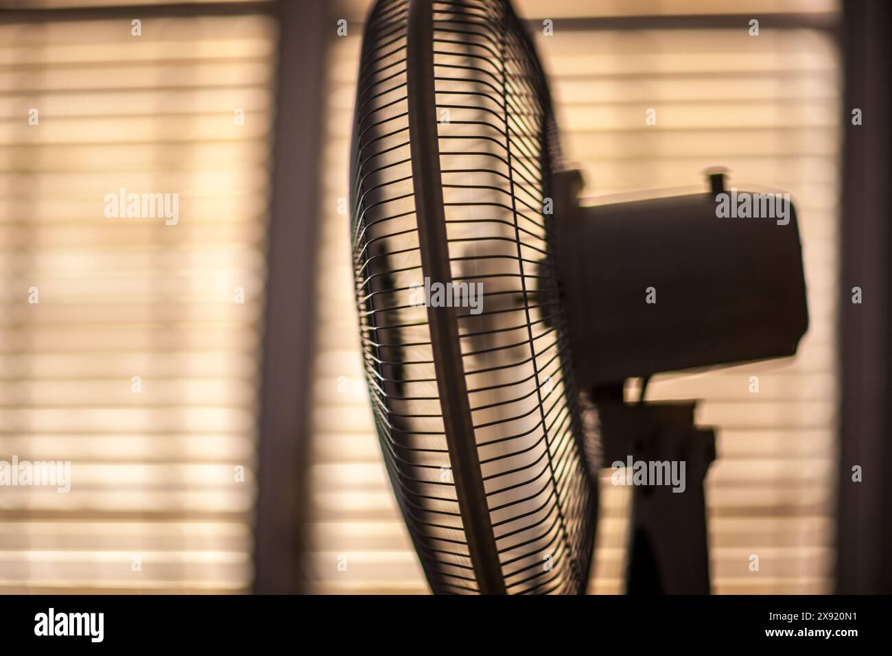 An electric fan running in a room with blinds down on a hot summer day ...
