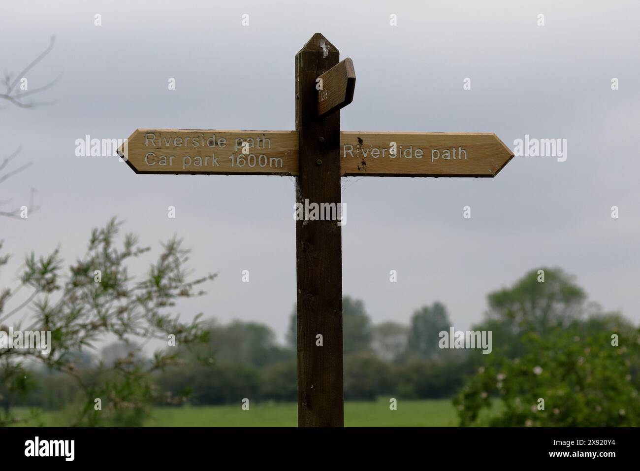 A wooden signpost with writing giving directions along a riverside path ...