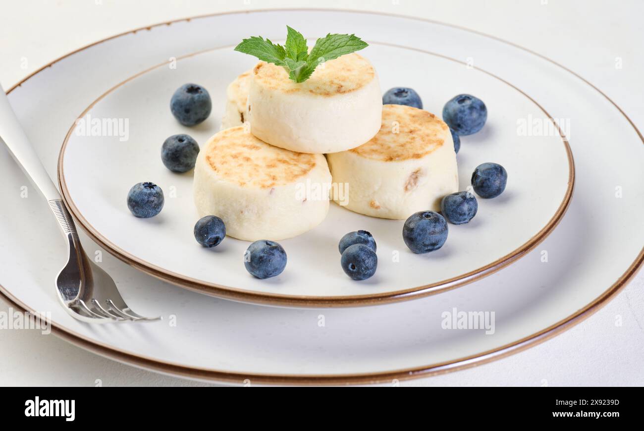 Round small fried cheesecakes on a plate with blueberries. Background ...