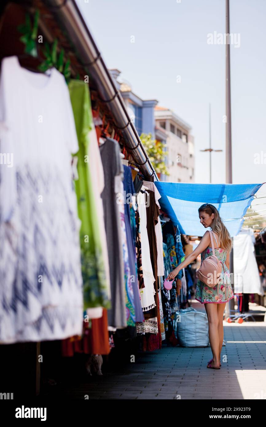 A young woman explores clothing options at a bustling street market ...