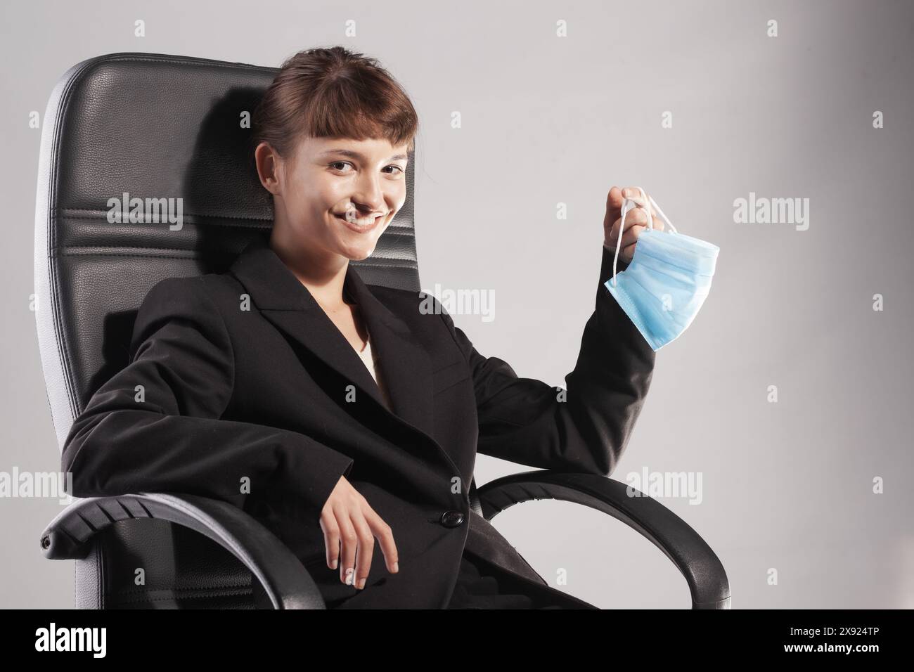 A young professional woman in a business suit sits on an office chair ...