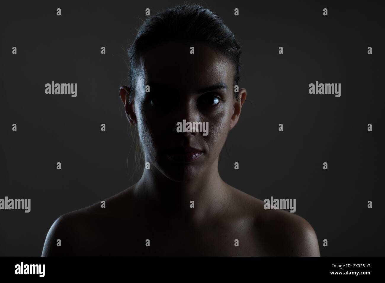 Artistic close-up of a young woman's face half-illuminated by dim light ...