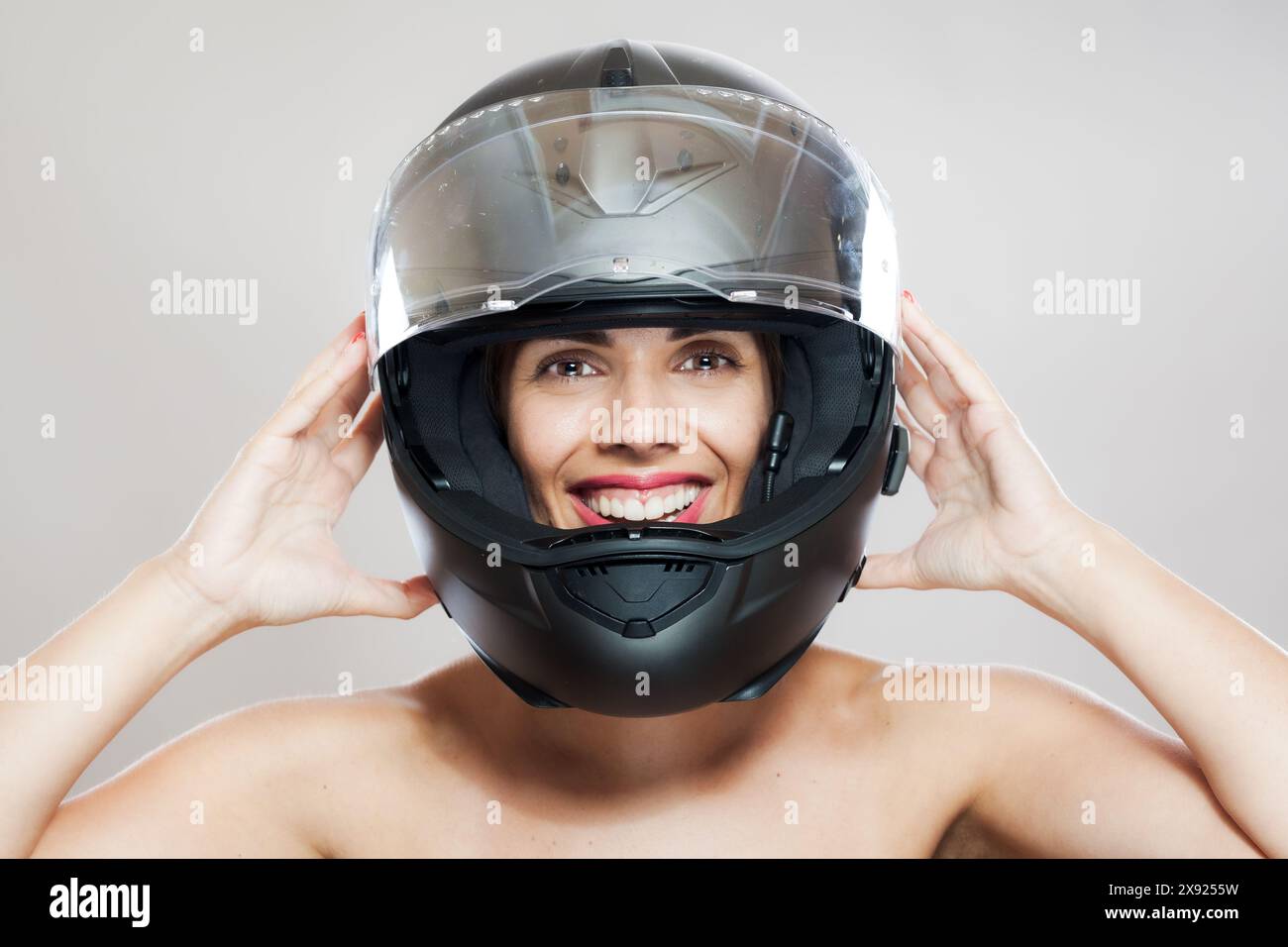 A cheerful woman adjusting her black motorcycle helmet, exuding safety ...